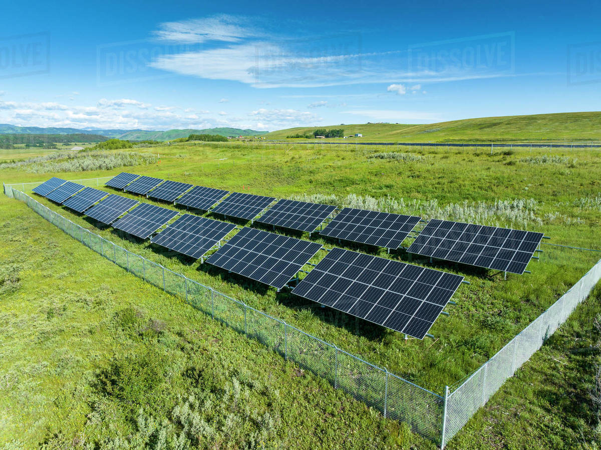 Two rows of solar panels in a green field with rolling hills in the ...