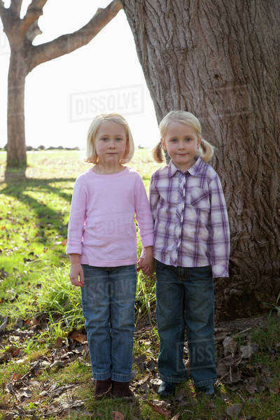 Two young girls with blond hair hold hands standing in front of a large ...