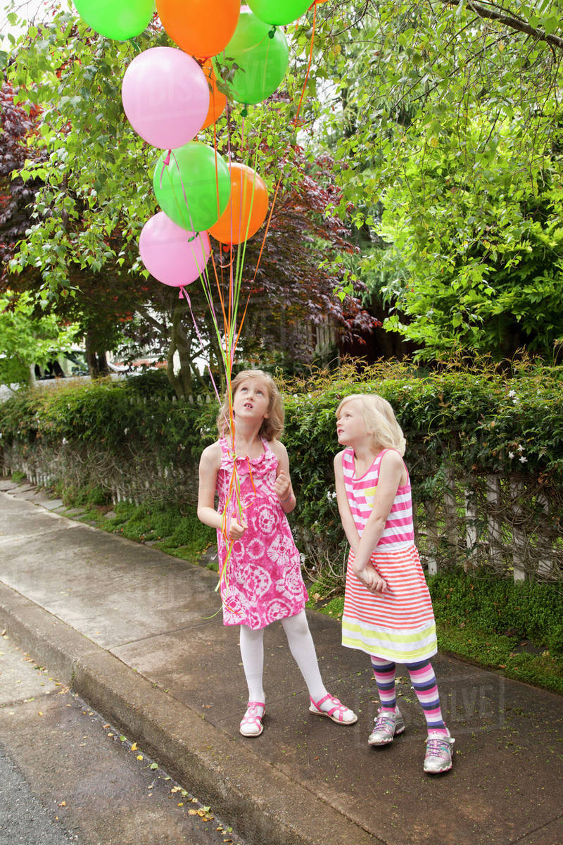 Two young girls standing on a sidewalk with a bouquet of balloons ...