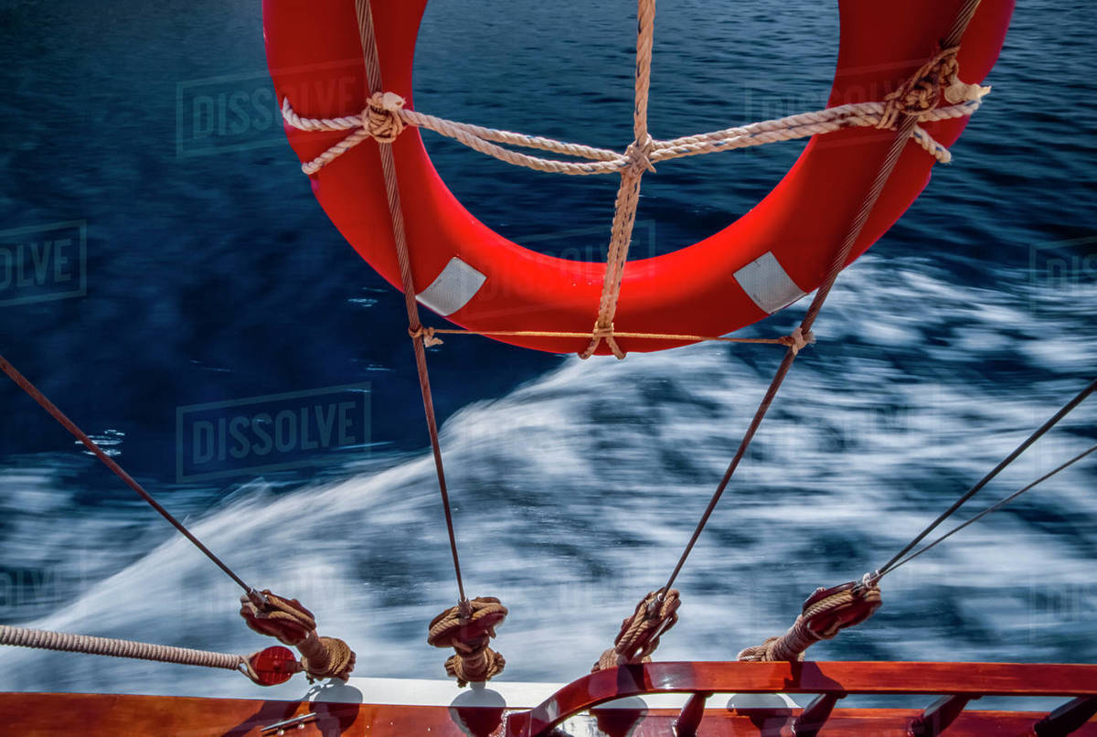 Starboard railing of boat, lines, life preserver, wake and blue sea ...