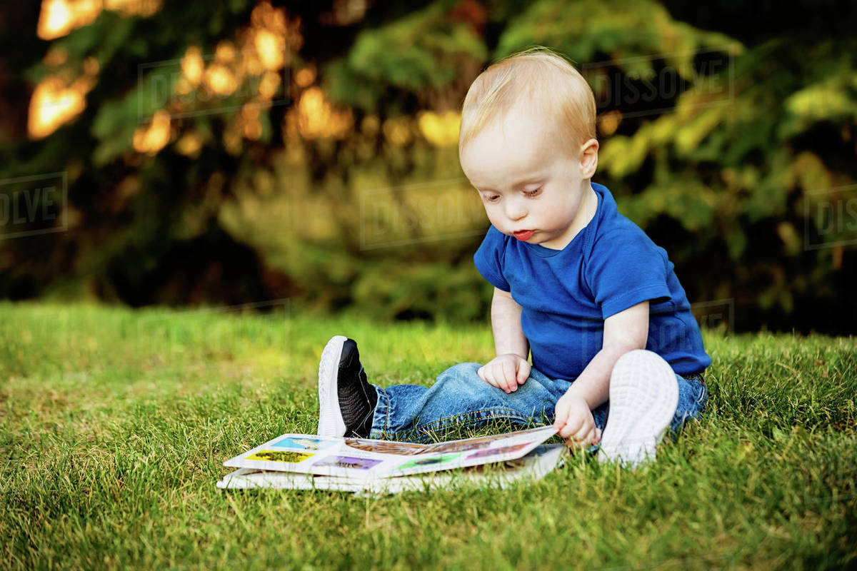 Baby boy with Down syndrome sitting and looking at a picture book on ...
