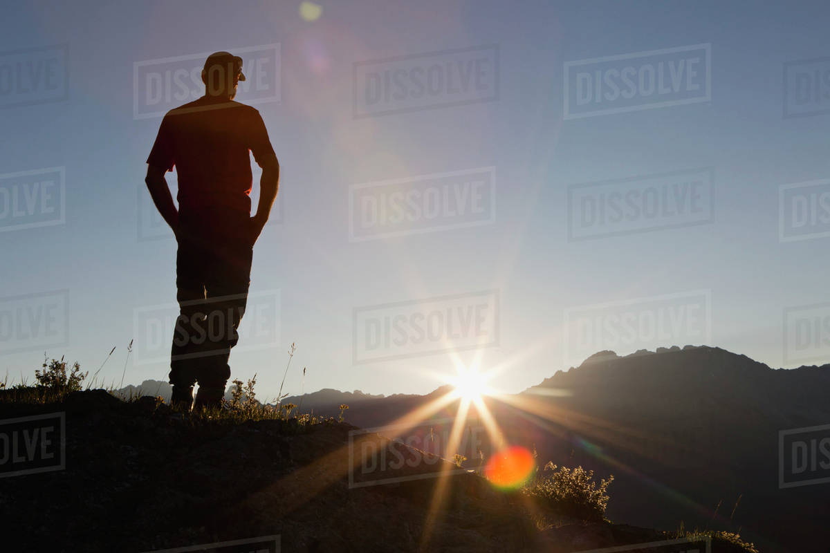 A Man Stands On A Ridge Overlooking The Landscape With Bright Sun Rays ...