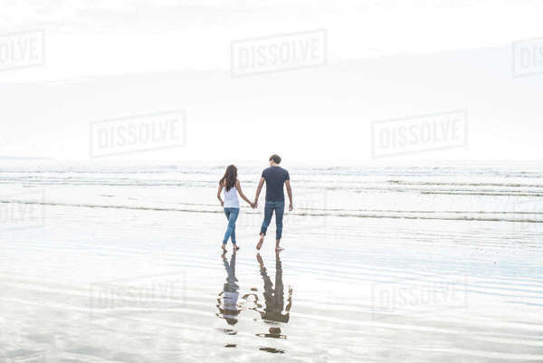 A young couple walk holding hands across the beach at Porthmadog ...