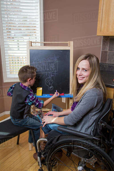 Young paraplegic mother teaching her son and drawing on a chalkboard ...