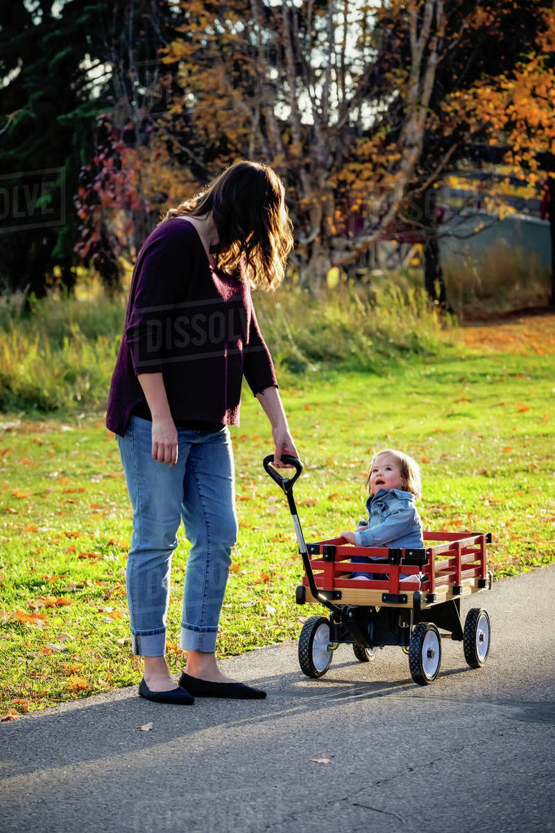A mother pulling her baby with Down Syndrome in a wagon in a city park ...