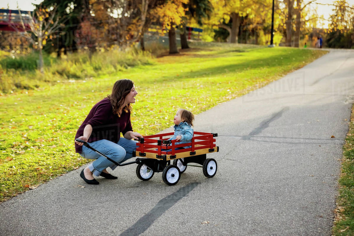 A mother pulling her baby with Down Syndrome in a wagon along a river ...