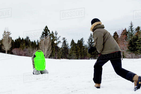A Man Throws Snowballs At Another Adult Who Is Holding A Sled To Block ...