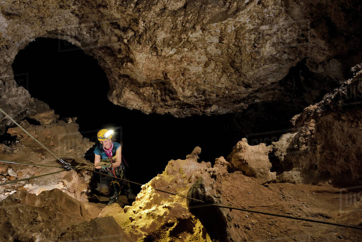 A cave explorer climbing up a rope inside a large vertical drop within ...