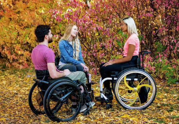 Group of three young paraplegics in their wheelchairs visiting together ...