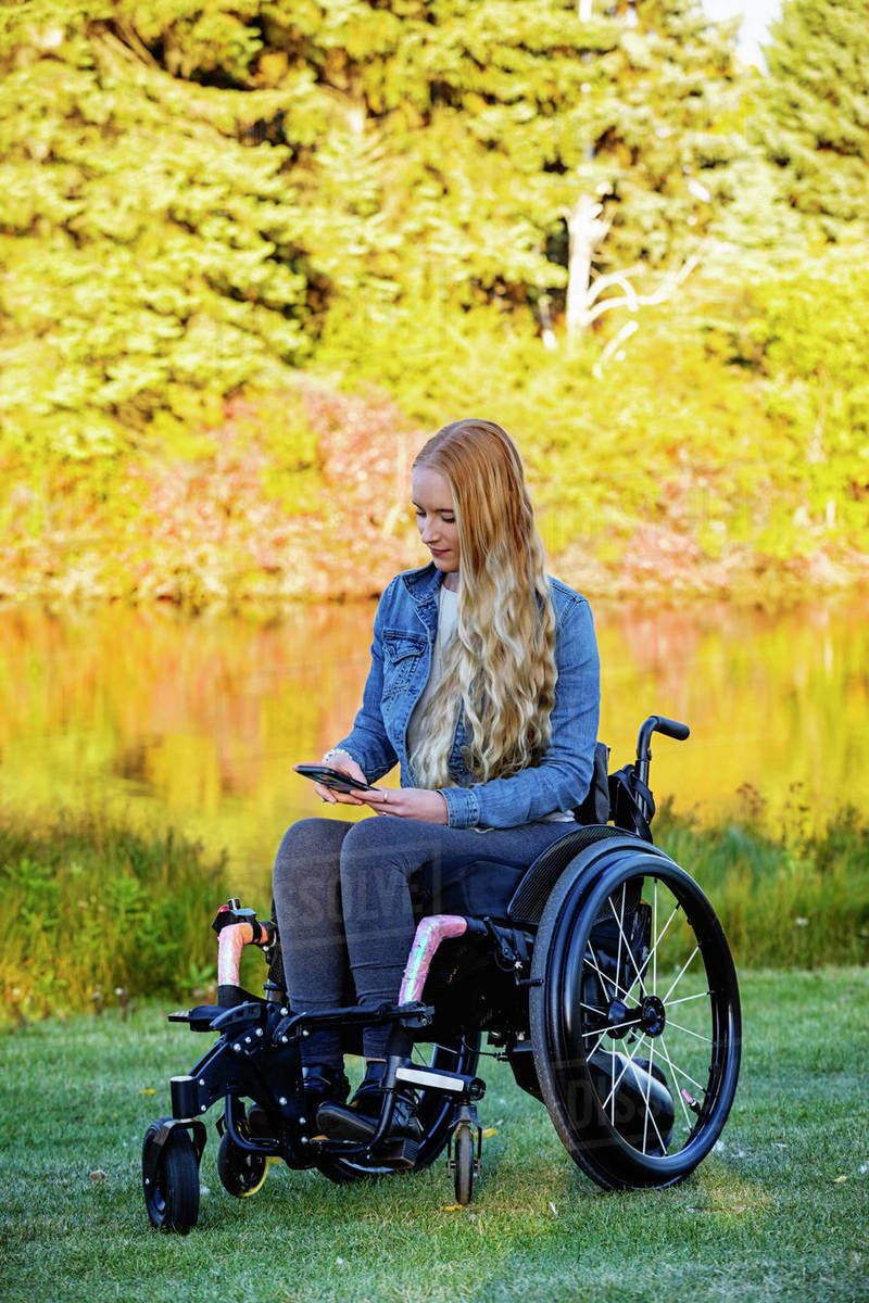 Young paraplegic woman in her wheelchair using a smart phone in a park ...