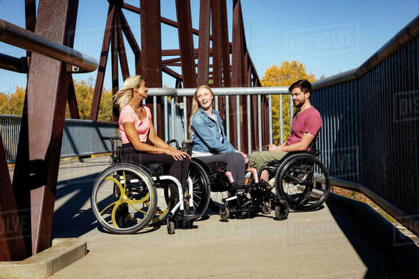 Group of three young paraplegics in their wheelchairs visiting together ...