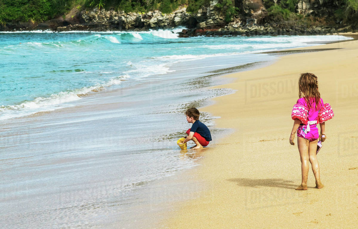 Children playing in the sand on D. T. Fleming beach at the water's edge; Kapalua, Maui, Hawaii ...