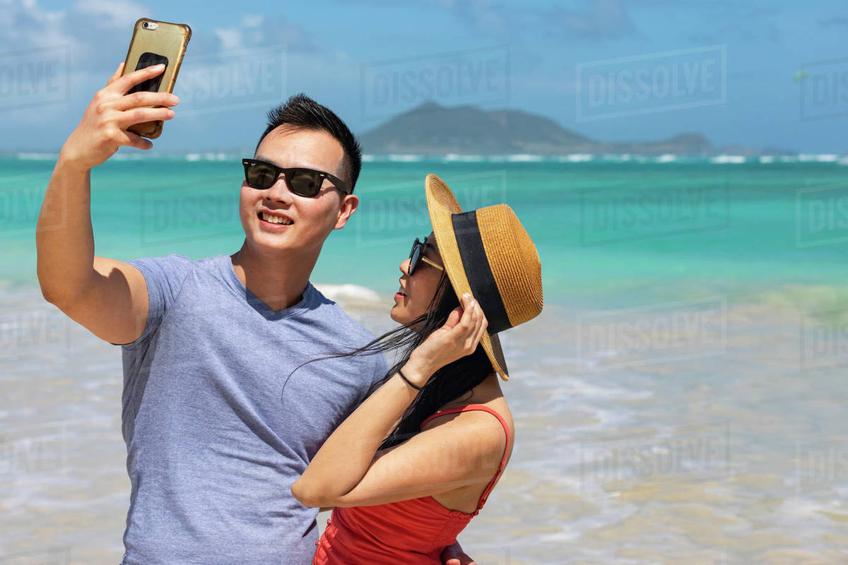 A couple takes a self-portrait while standing in the ocean surf while ...