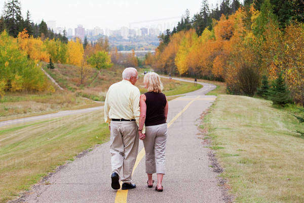 Mature married couple walking together in park during fall season ...