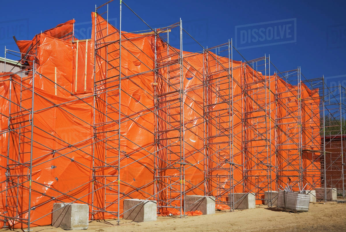 A commercial building is covered up with an orange tarp during ...
