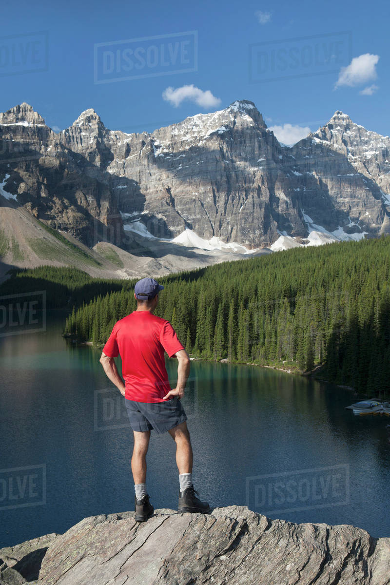 Male Standing On Cliff Lookout Overlooking A Lake And Mountain Range ...