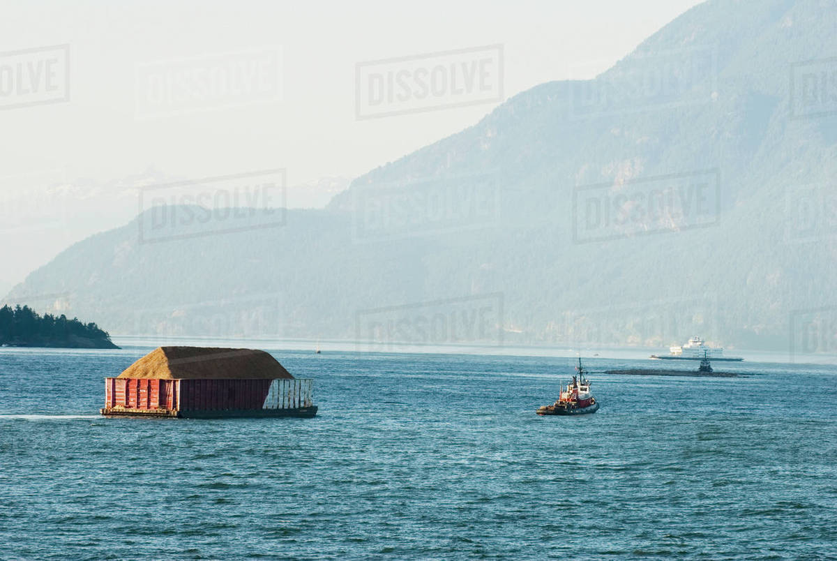 Tug Boat Pulling Logs Through The Ocean With Mountains In The ...