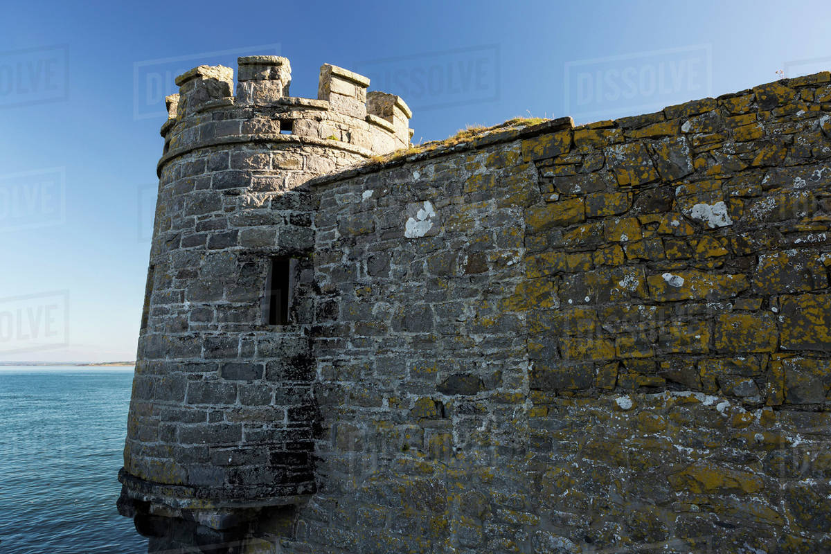 Stone wall with turret at water's edge and blue sky; Carrigaholt ...