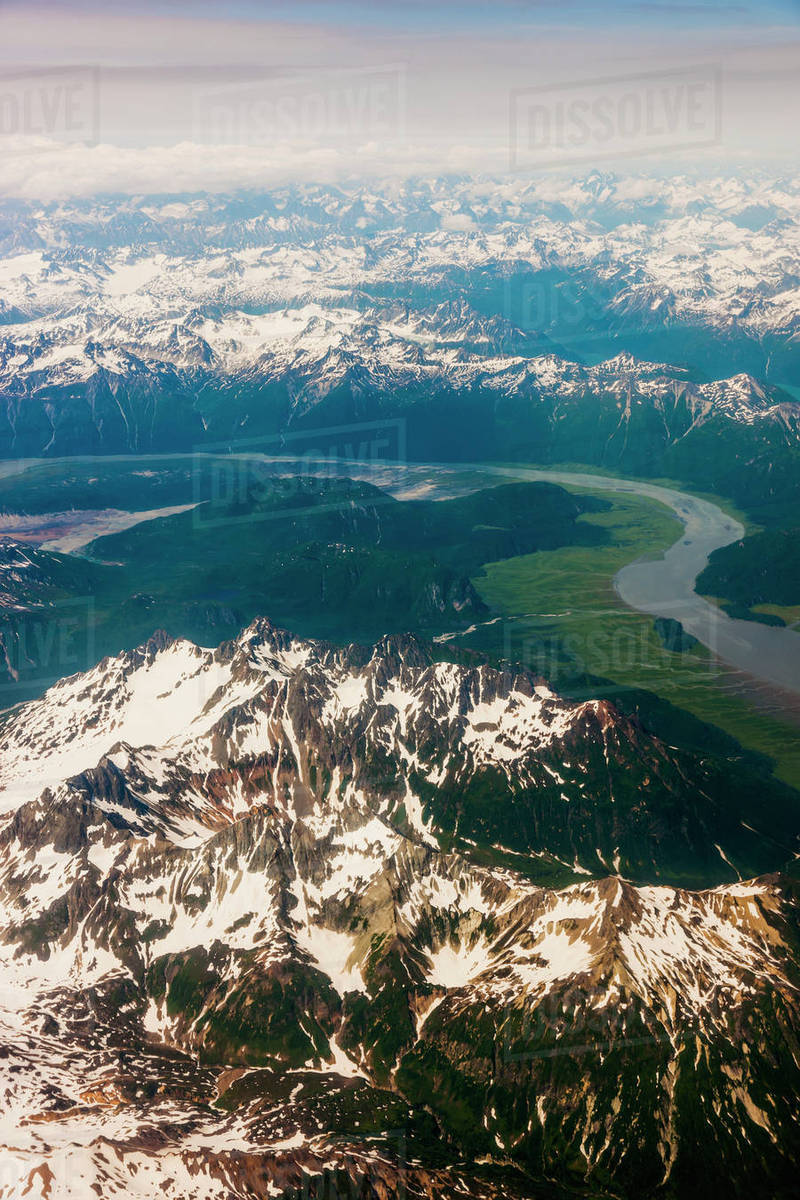 Aerial view of snow-capped peaks surrounding a green river valley ...