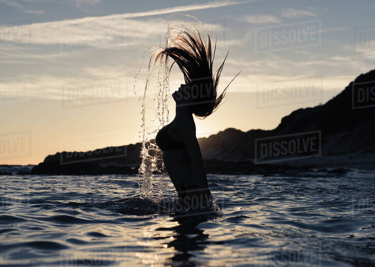Silhouette of a woman in waist-deep water flipping her wet long hair up ...
