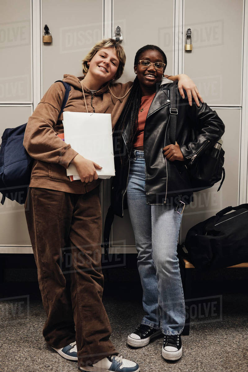 Full length portrait of smiling teenage girl standing with arm around ...