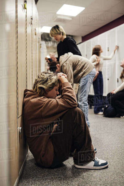 Side view of depressed teenage girl sitting by locker in school ...