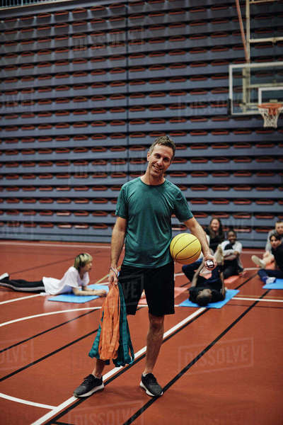 Full length portrait of smiling male coach standing with basketball ...