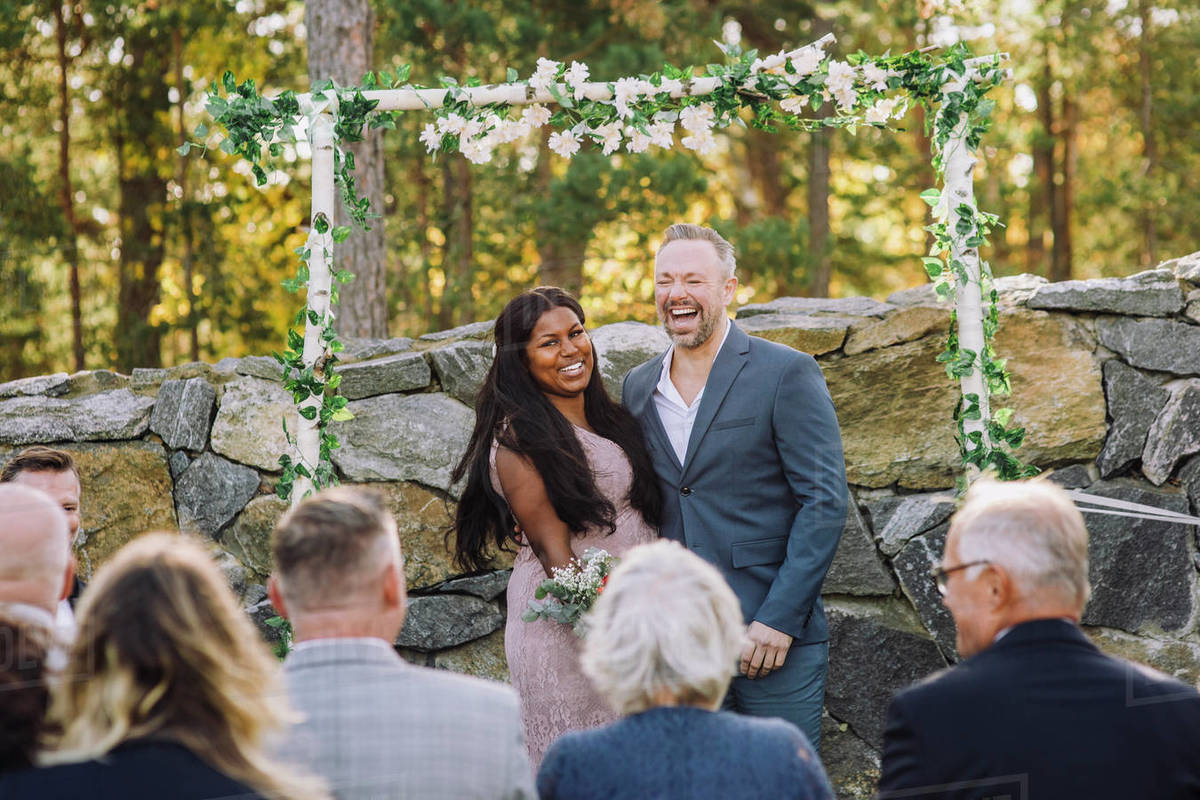 Happy newlywed multiracial couple looking at guest during wedding ...