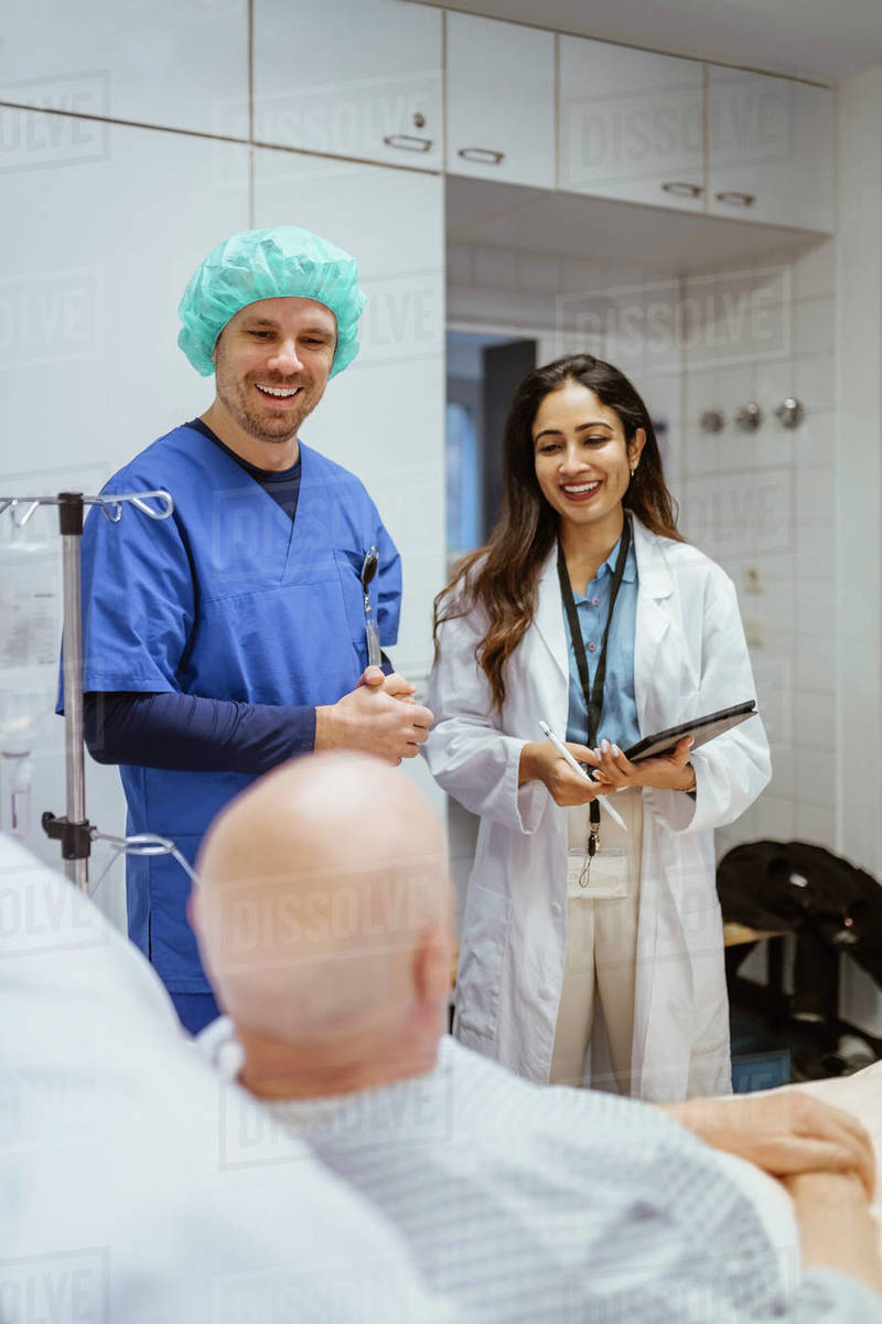 Happy healthcare workers talking to senior male patient in hospital ...