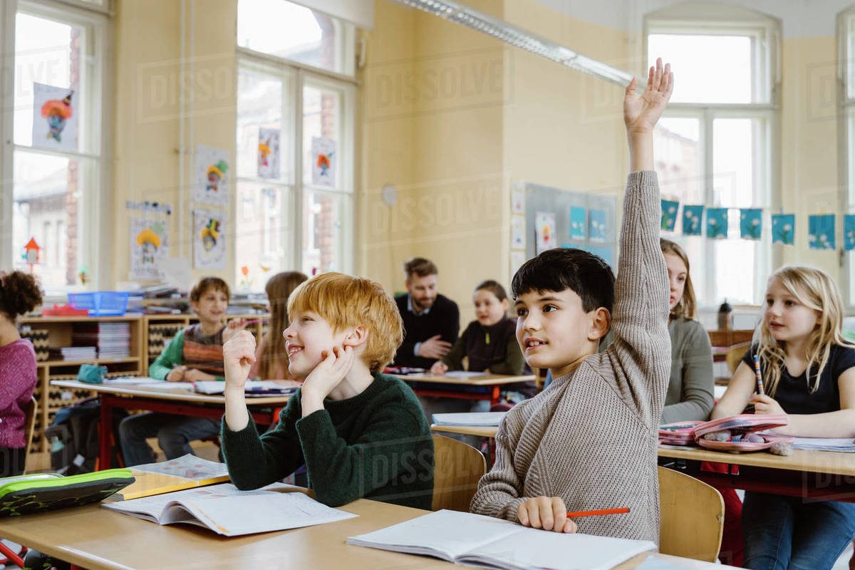 Boy with hand raised answering during lecture while sitting by male ...