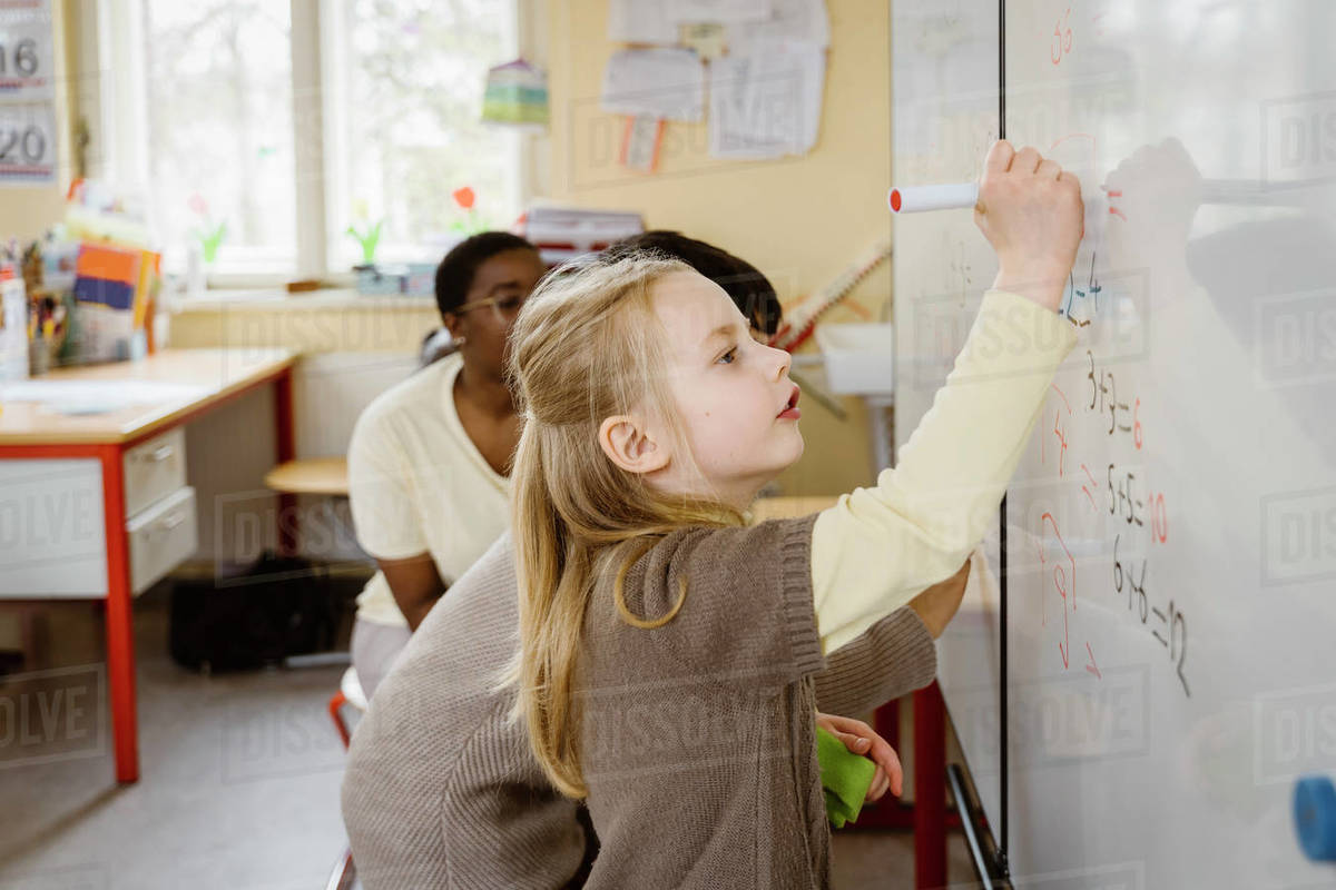 Blond girl solving maths problem while writing on whiteboard in ...