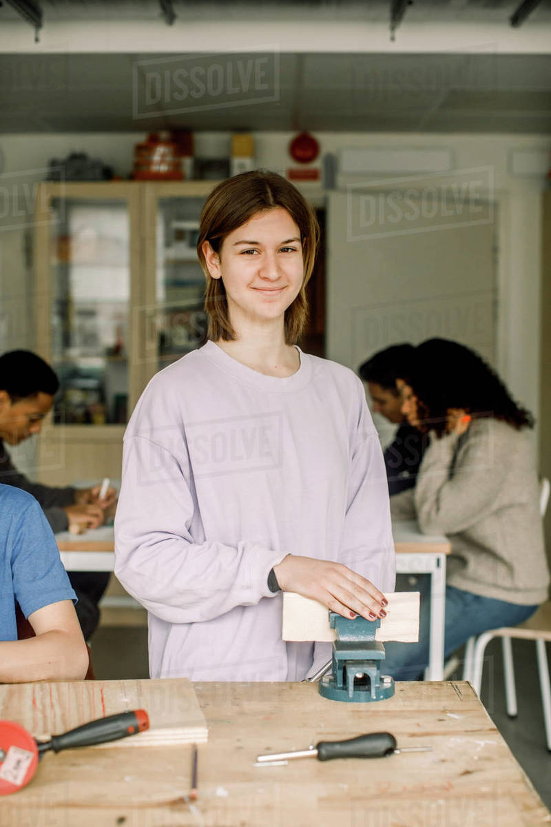 Portrait of smiling female teenage student fixing wood on clamp during ...