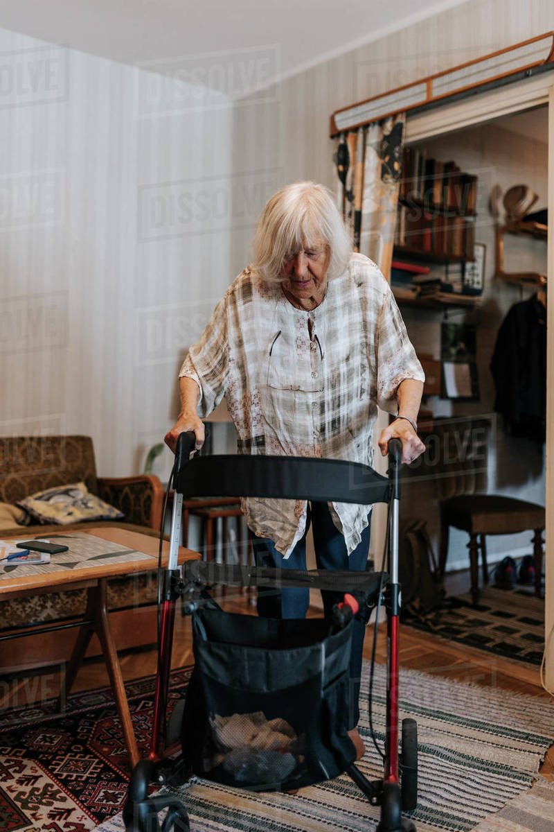 Senior woman walking at home using mobility walker - Stock Photo - Dissolve