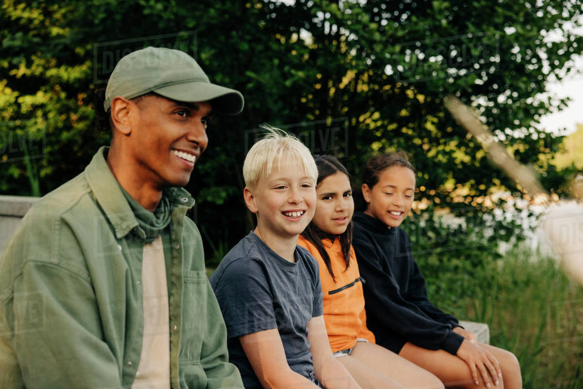 Kids sitting with smiling counselor wearing cap at summer camp ...