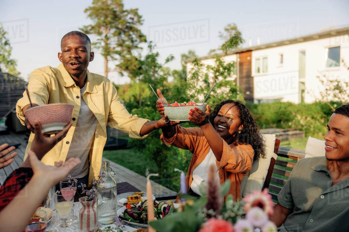 Young man serving food to friends during dinner party in back yard ...