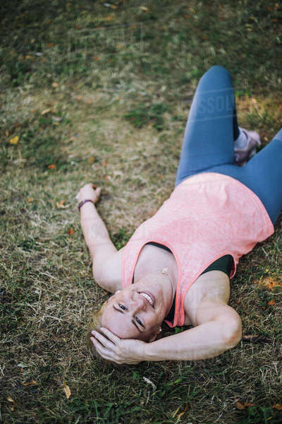 Portrait of smiling woman with head in hand lying down on grass at park ...
