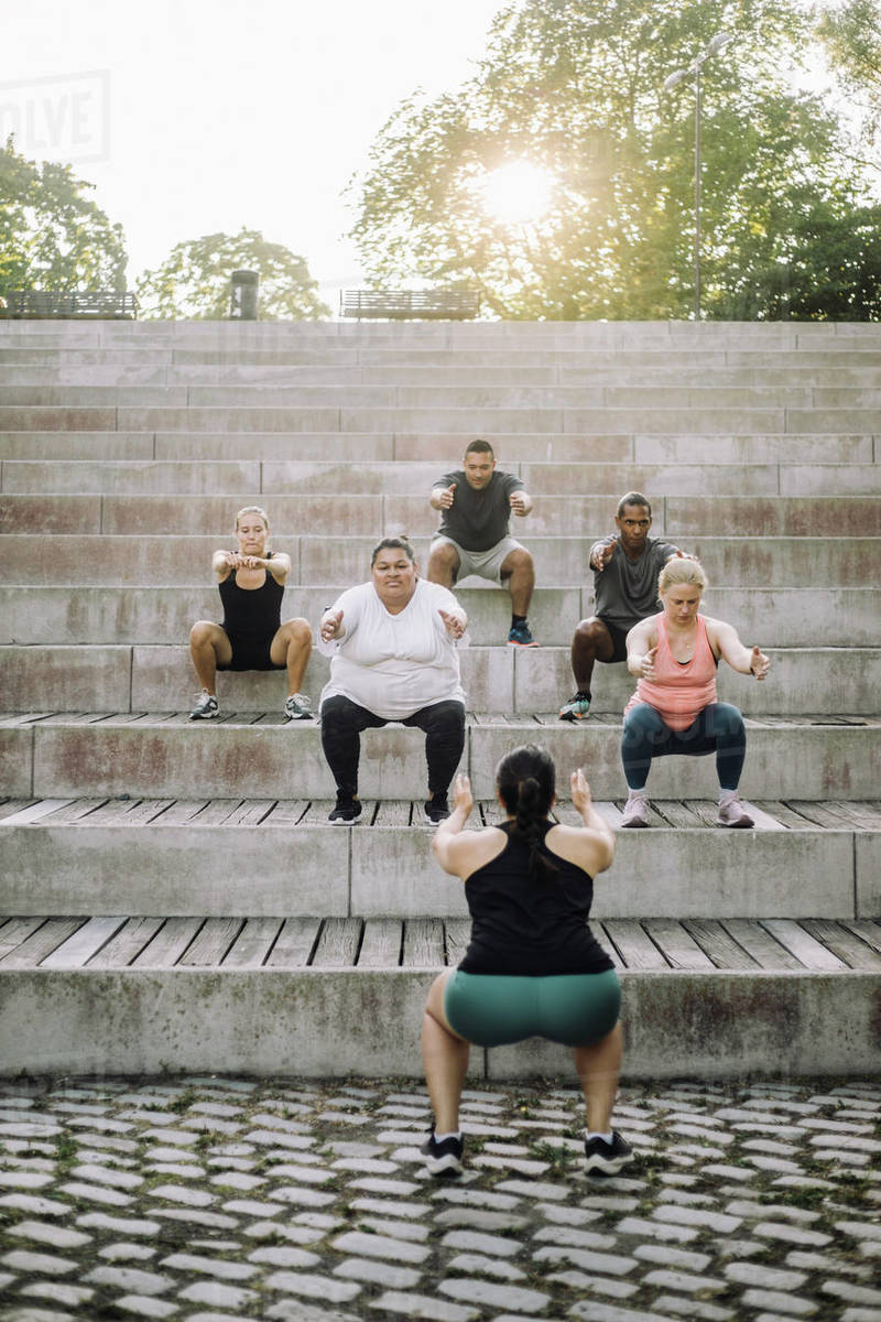 Team doing squats on steps with female fitness instructor at park ...