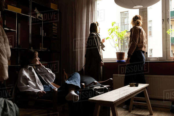 Friends looking through window with woman sitting on chair in apartment ...