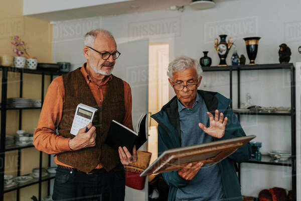 Senior male customer buying picture frame from salesman at antique shop ...
