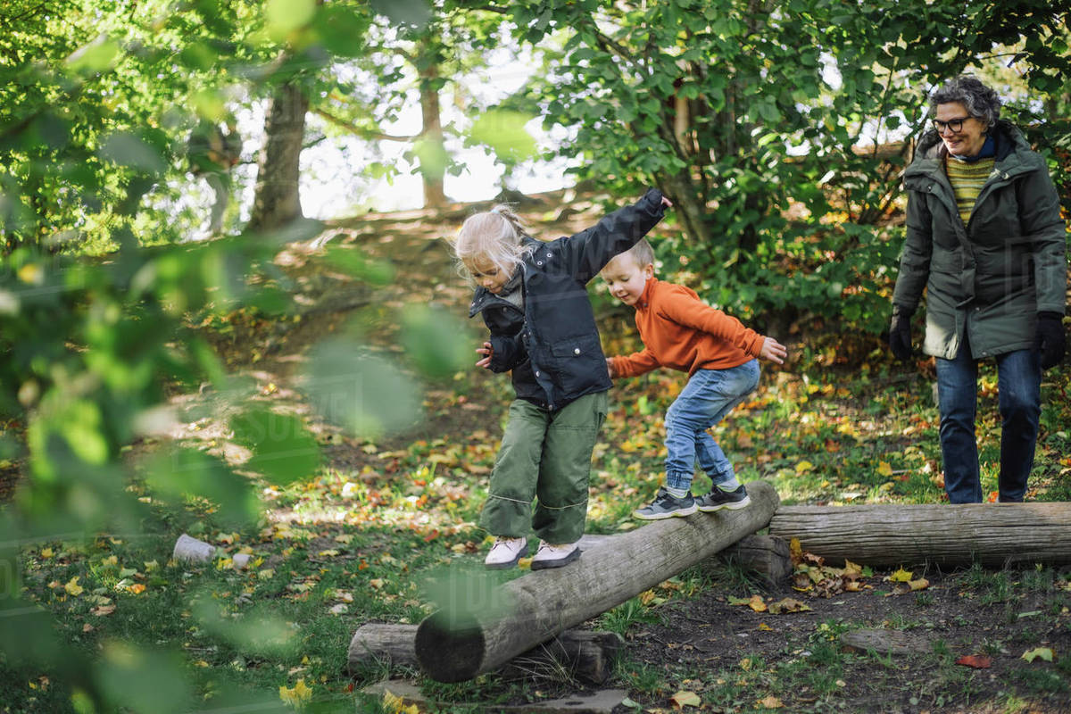 Female teacher looking at children balancing on wooden logs while ...