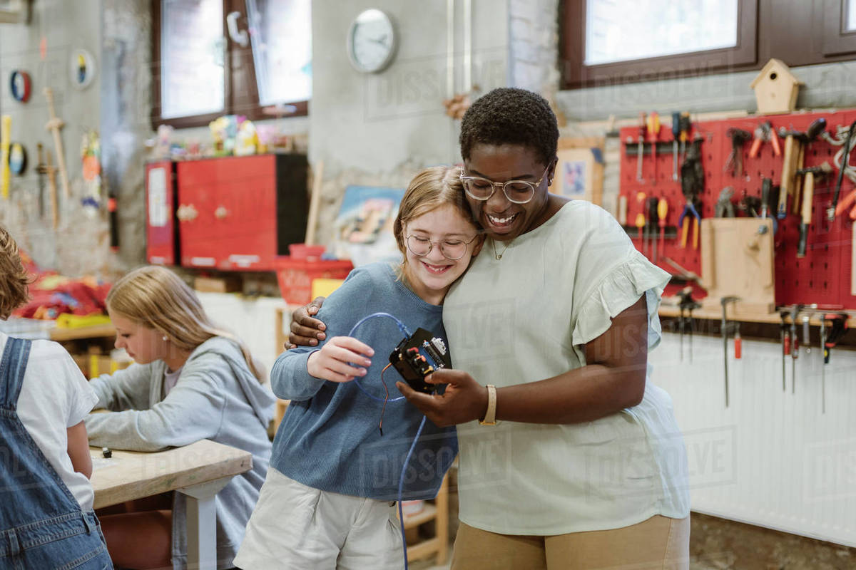 Happy female teacher appraising student while holding electrical part ...