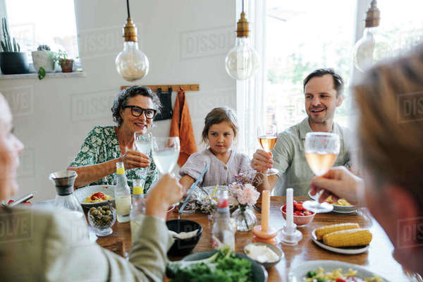 Happy multi-generational family toasting drinks while sitting at dining ...