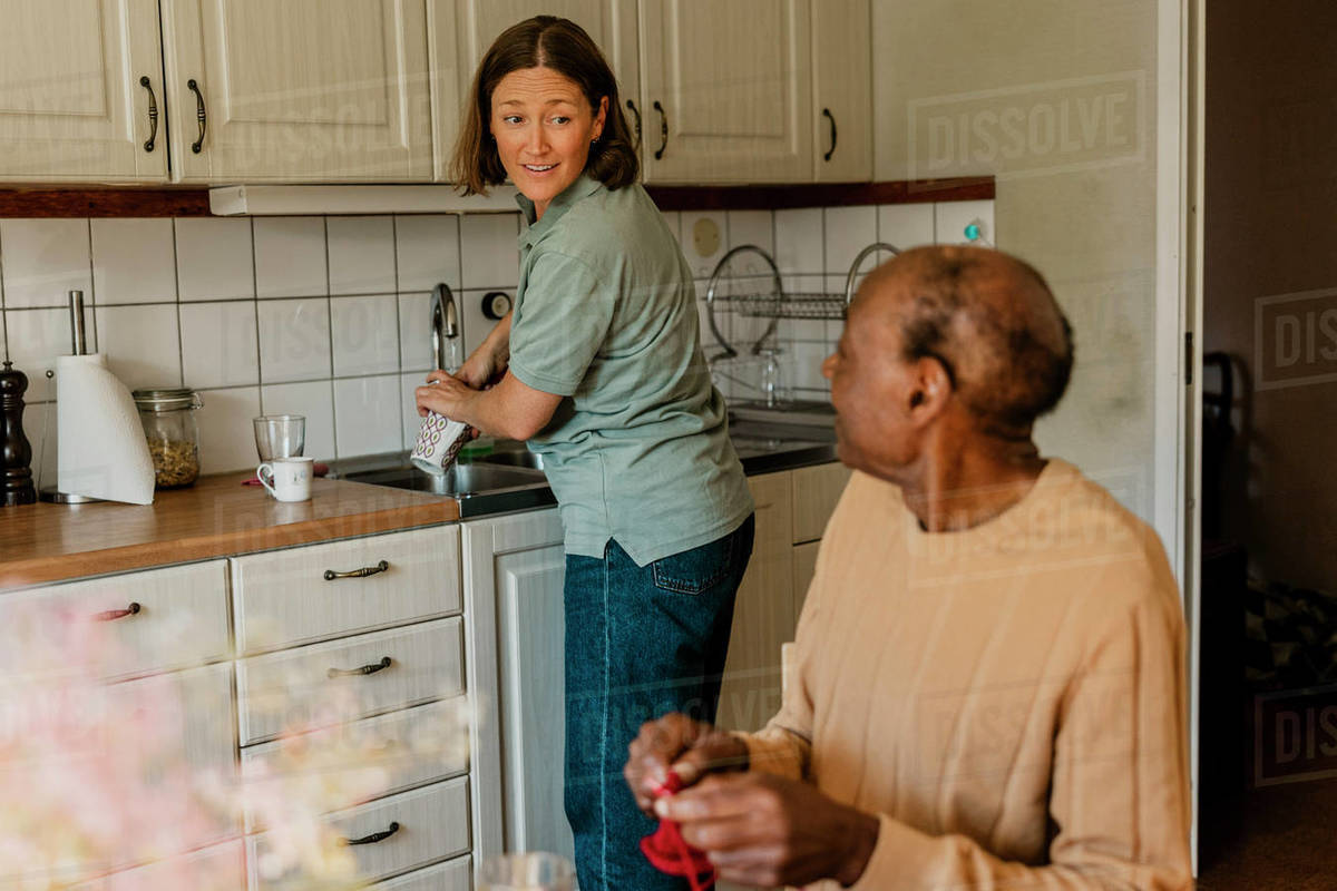 Female nurse washing dishes and while talking with senior man sitting ...