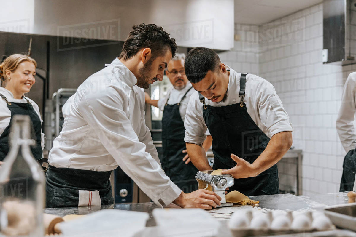 Young male chef helping colleague in using pasta maker on kitchen ...