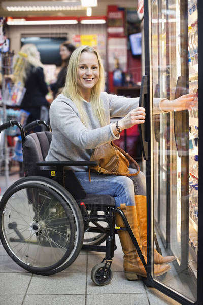 Portrait of happy disabled woman in wheelchair at refrigerated section ...