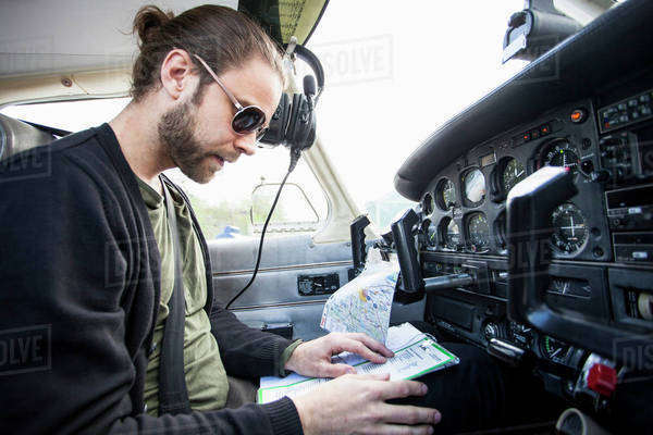 Side view of mid adult pilot with clipboard sitting in cockpit of ...
