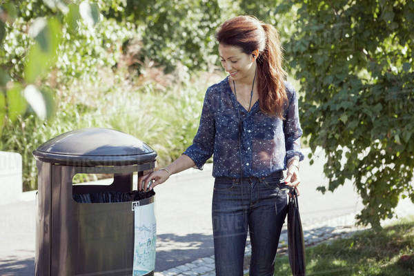 Businesswoman throwing garbage in bin at park - Stock Photo - Dissolve