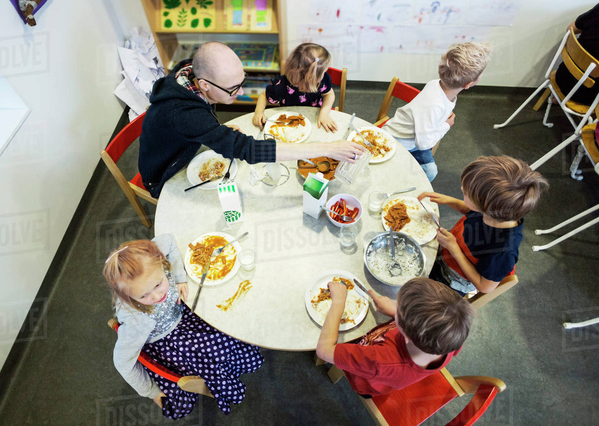 High angle view of kindergarten students and teacher having food at ...