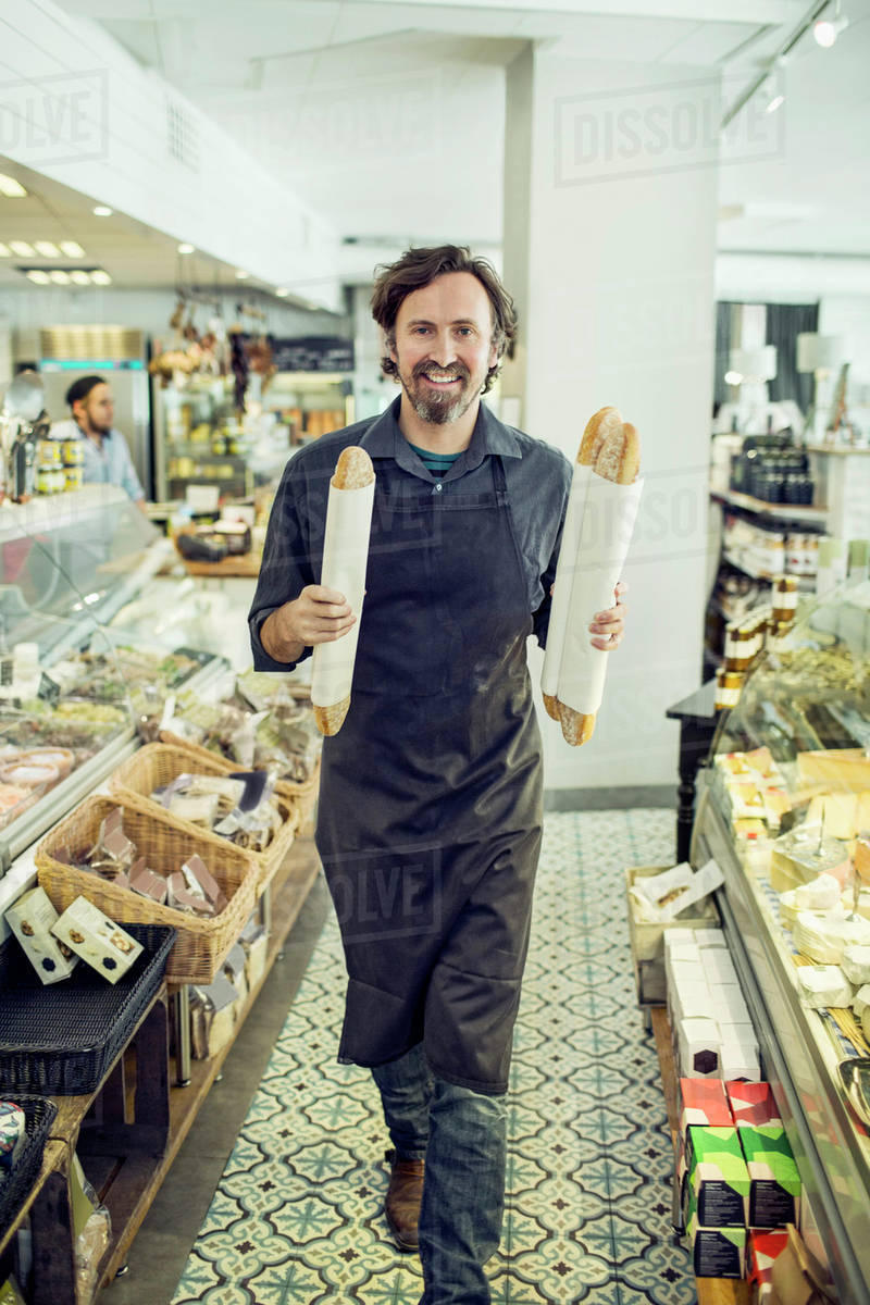 Portrait of mature male baker with loaves of bread walking in ...