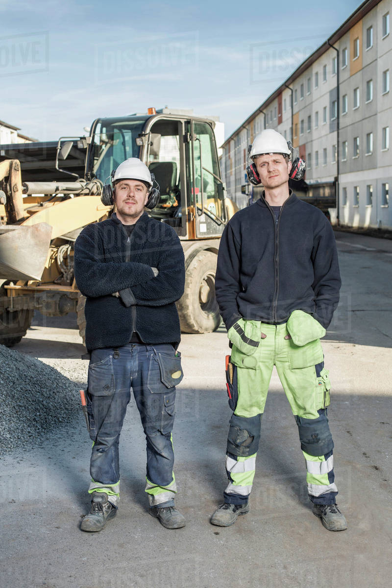 Full length portrait of confident workers standing at construction site ...